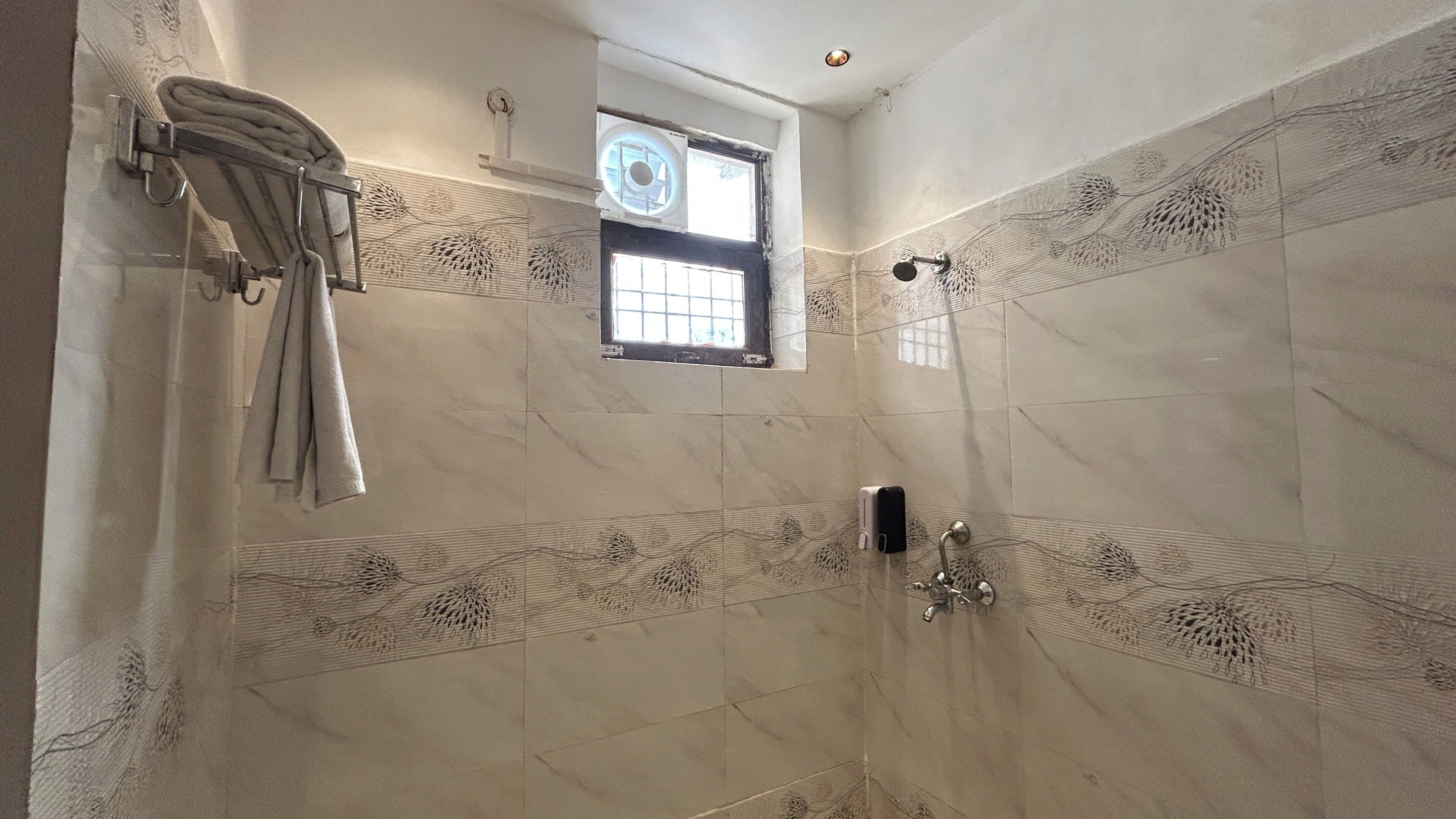 Casa de banho com chuveiro, toalheiro, janela e azulejos estampados.