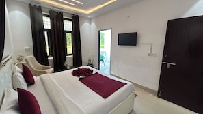 Quarto de hotel com cama, cadeira, televisão e porta.