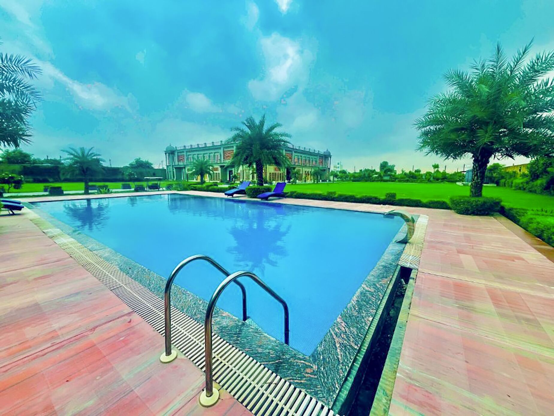 Piscina com deck ladrilhado, espreguiçadeiras e um prédio grande ao fundo.
