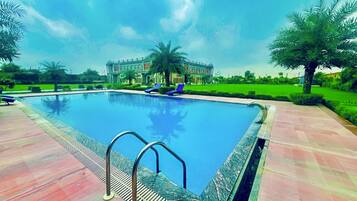 Piscina com deck ladrilhado, espreguiçadeiras e um prédio grande ao fundo.