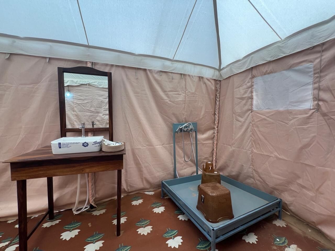 Interior de uma tenda com uma mesa, um espelho, um sanitário portátil e um dispensador de água.