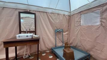 Interior de uma tenda com uma mesa, um espelho, um sanitário portátil e um dispensador de água.