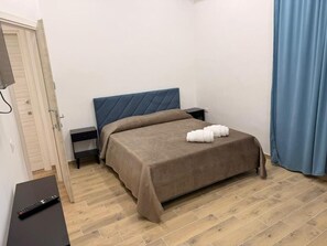 Quarto com uma cama, mesa de cabeceira, um controle remoto sobre a mesa e cortina azul.