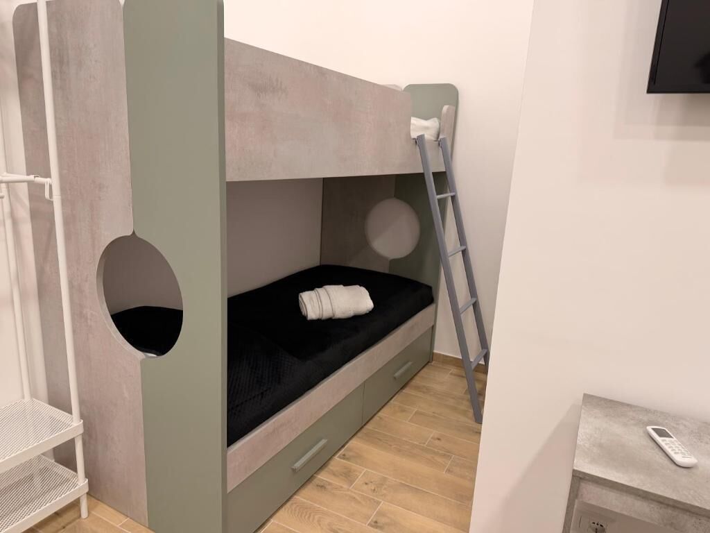 Uma cama beliche com escada, uma pequena prateleira e uma televisão fixada na parede.