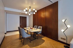 Uma sala de jantar moderna com piso de madeira, uma mesa redonda com cadeiras e um lustre contemporâneo acima.