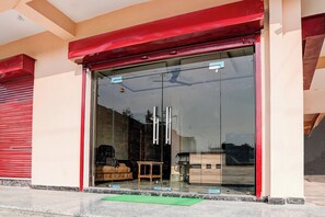 Fachada de loja com porta de vidro, toldo vermelho e tapete verde no chão.
