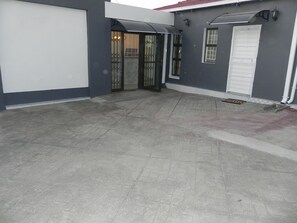 Um pátio com piso de azulejos, uma porta branca e uma janela com portão de metal.