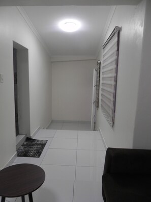 Um corredor com piso de azulejos, uma mesa redonda e um sofá de cor escura.