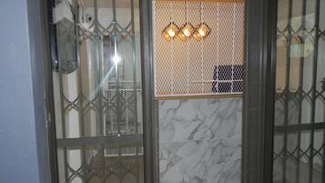 Quarto com parede de mármore, portão de metal e janela iluminada.