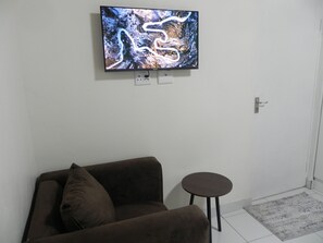 Um quarto com um sofá marrom, uma mesa redonda pequena e uma televisão de tela plana na parede.