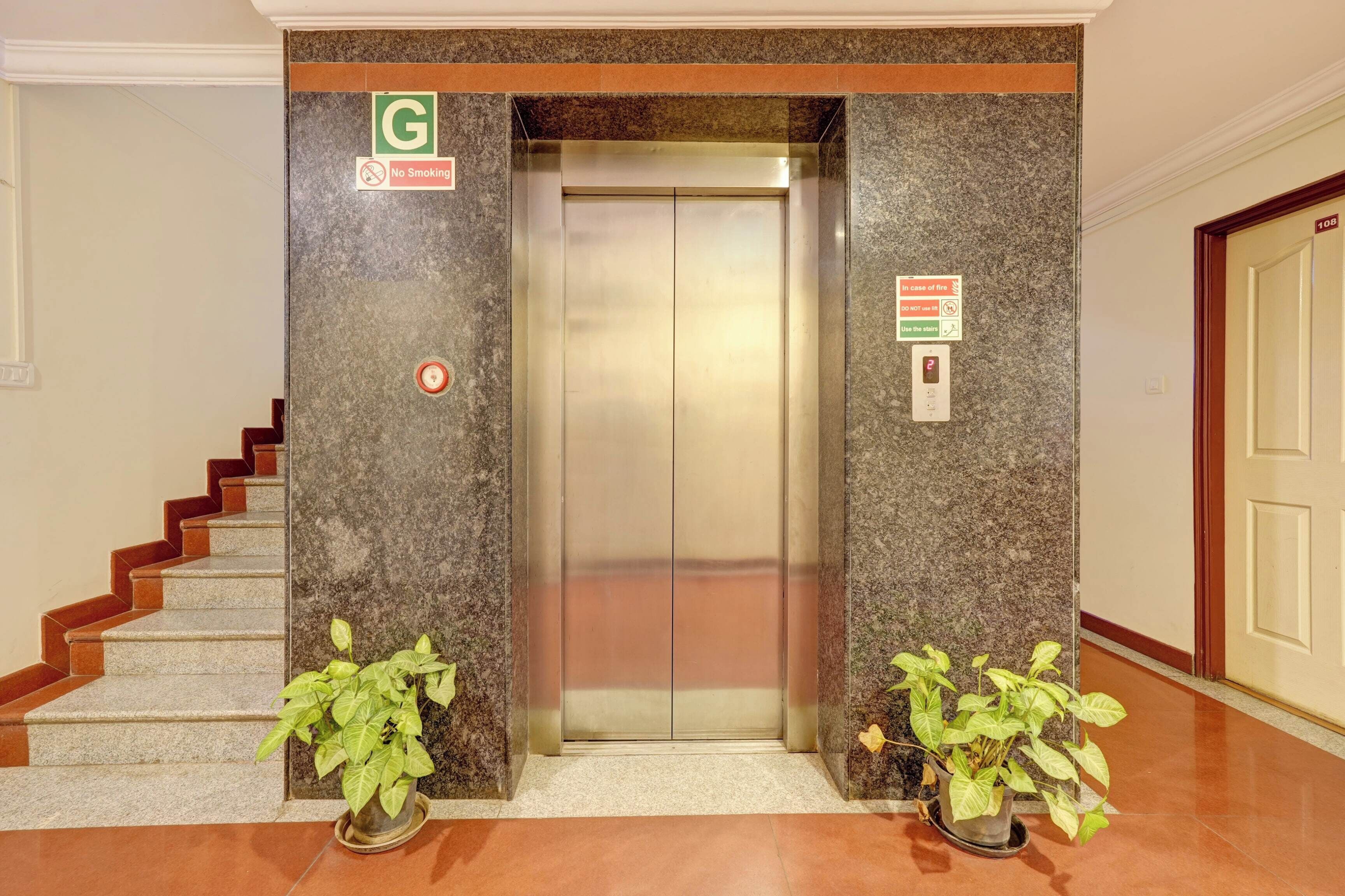 Um elevador com placa de 'Não Fumar', aviso de segurança contra incêndio e um 'G' indicando banheiro unissex.