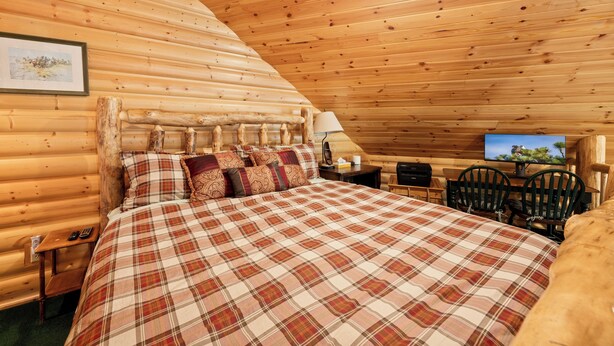 Quarto de cabana de tronco com uma cama, uma escrivaninha e uma televisão.