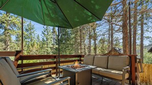 Um deck externo com lareira, assentos e vista para uma floresta.