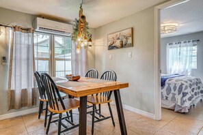 Uma área de refeições com mesa de madeira, cadeiras pretas, luminária pendente e um quadro na parede.