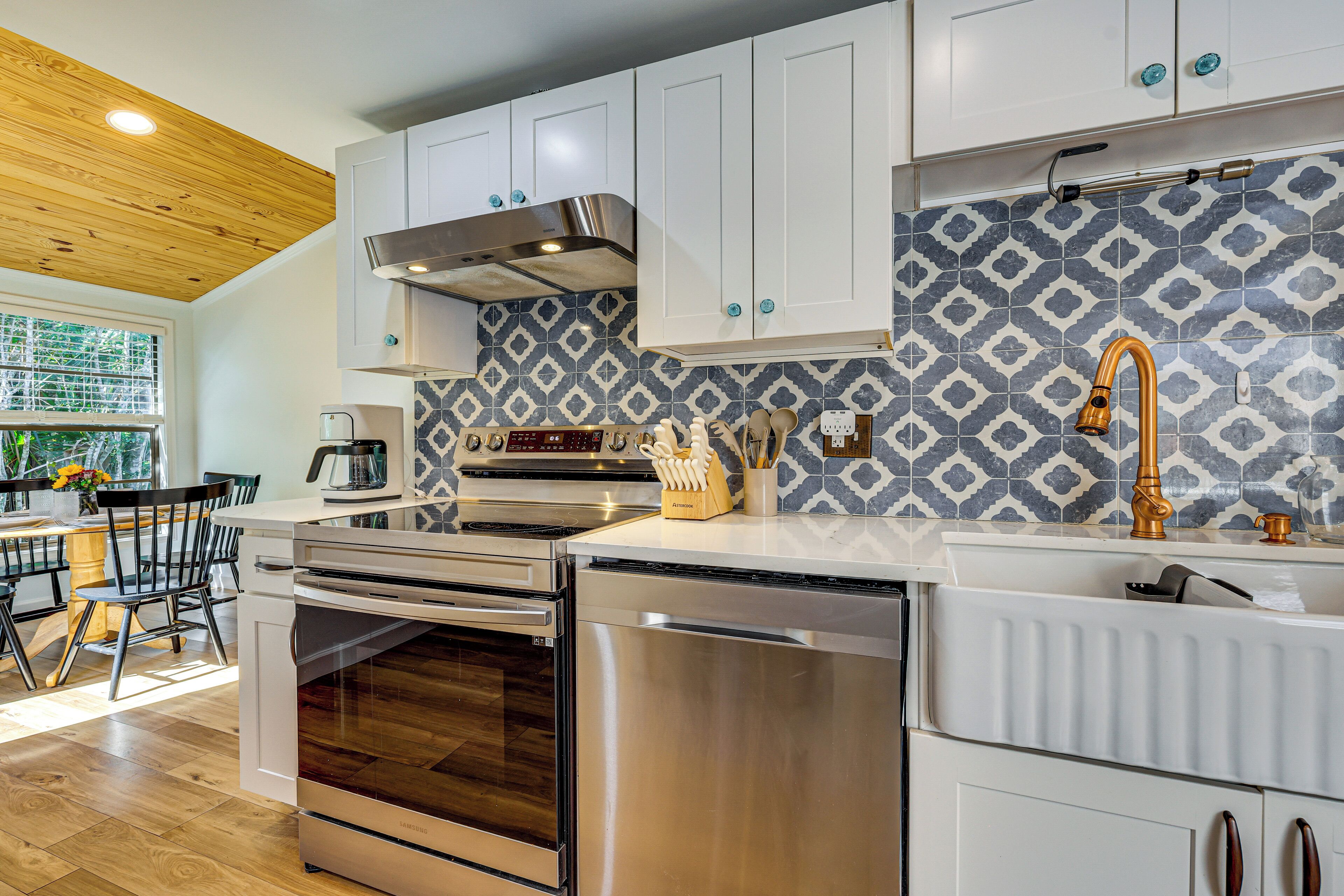 Cozinha moderna com eletrodomésticos de aço inoxidável, armários brancos e azulejos de parede estampados.