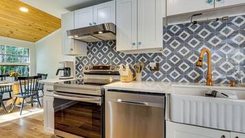 Cozinha moderna com eletrodomésticos de aço inoxidável, armários brancos e azulejos de parede estampados.