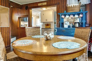 Uma mesa de jantar de madeira com quatro jogos americanos, uma tigela de vidro com pão e um armário azul com eletrodomésticos de cozinha.