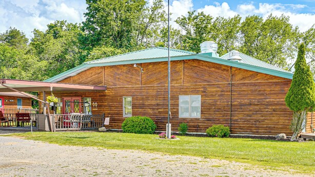 Uma cabana de madeira rústica com telhado verde, um mastro com a bandeira americana e um pequeno alpendre com área de estar externa.