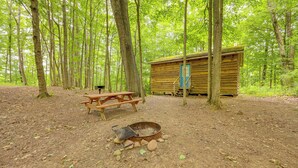 Uma cabana rústica com mesa de piquenique e lareira em meio à floresta.