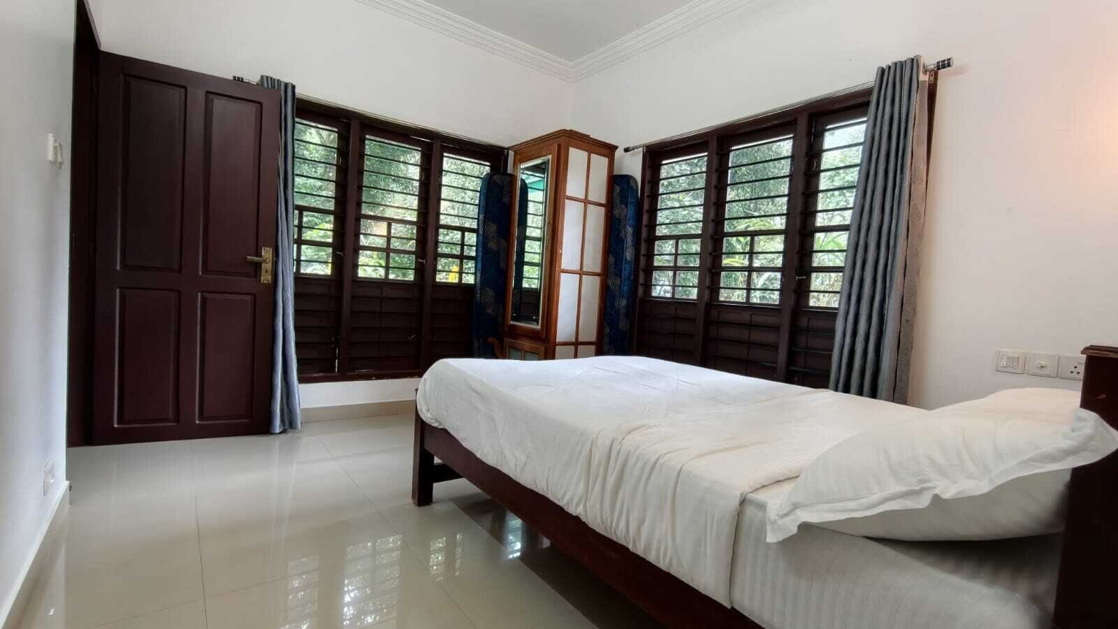 Um quarto com cama, guarda-roupa e janela com cortinas.