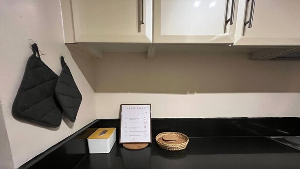 Uma bancada de cozinha com uma caixa branca, um quadro com as regras da casa e uma cesta de palha.
