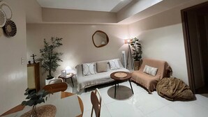 Sala de estar com sofá, mesa de centro e cadeiras. Há uma planta, um abajur e um ventilador de teto.