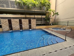 Piscina com piso de azulejos, cercada por um muro de pedra e um guarda-corpo de metal.