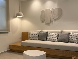 Uma sala de estar moderna com um sofá, almofadas estampadas, um banquinho redondo e uma luminária pendente.