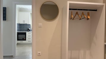 Quarto com um guarda-roupa branco, um espelho redondo e um cabideiro com ganchos.