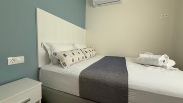 Quarto de hotel com cama, mesa de cabeceira, ar-condicionado fixado na parede e tomada.