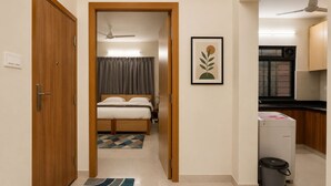 Quarto de hotel com cama, banheiro, cozinha compacta e porta que dá acesso a outro cômodo.