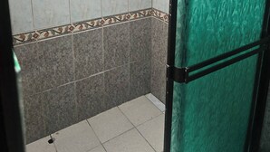Casa de banho com chuveiro, paredes azulejadas, dispensador de sabonete e cortina verde.