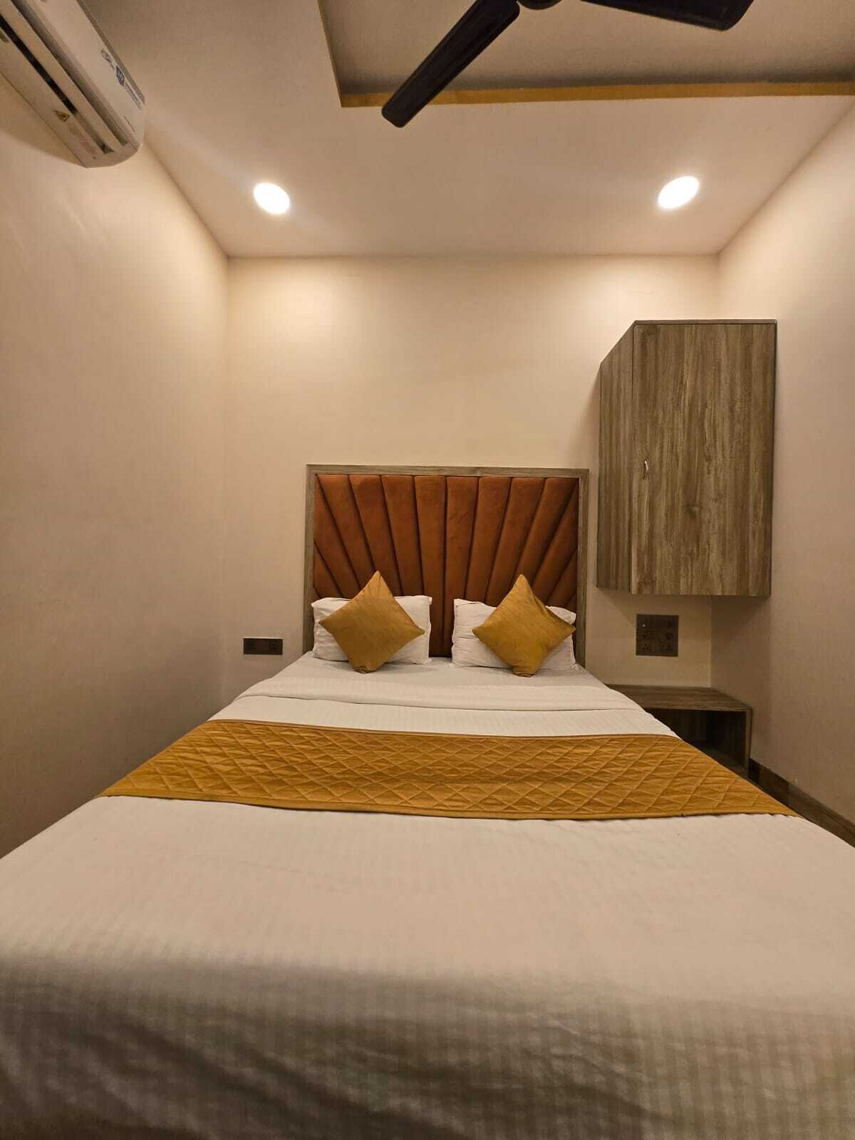 Quarto de hotel com cama, cabeceira de madeira, mesa de cabeceira e armário fixado na parede.
