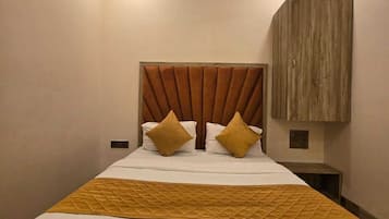 Quarto de hotel com cama, cabeceira de madeira, mesa de cabeceira e armário fixado na parede.