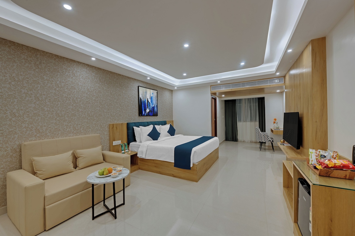 Quarto de hotel moderno com cama, sofá, uma mesinha com frutas e televisão.