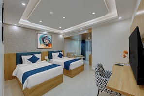 Quarto de hotel com duas camas, uma escrivaninha, televisão e um quadro na parede.