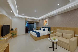 Quarto de hotel moderno com uma cama, um sofá, uma TV e uma pequena mesa com um vaso e maçãs.