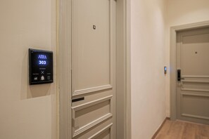 Corredor com fechadura digital exibindo 'AJIRA 303' e opções para 'Limpeza do Quarto' e 'Lavanderia'.