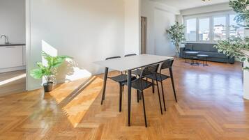 Uma sala de estar ampla com mesa e cadeiras de jantar, sofá e uma grande janela com vista para a cidade.