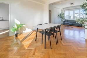 Uma sala de estar ampla com mesa e cadeiras de jantar, sofá e uma grande janela com vista para a cidade.