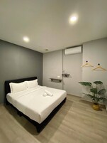 Quarto de hotel moderno com uma cama grande, uma mesa de cabeceira, um aparelho de ar condicionado, uma pequena prateleira e um vaso de plantas.