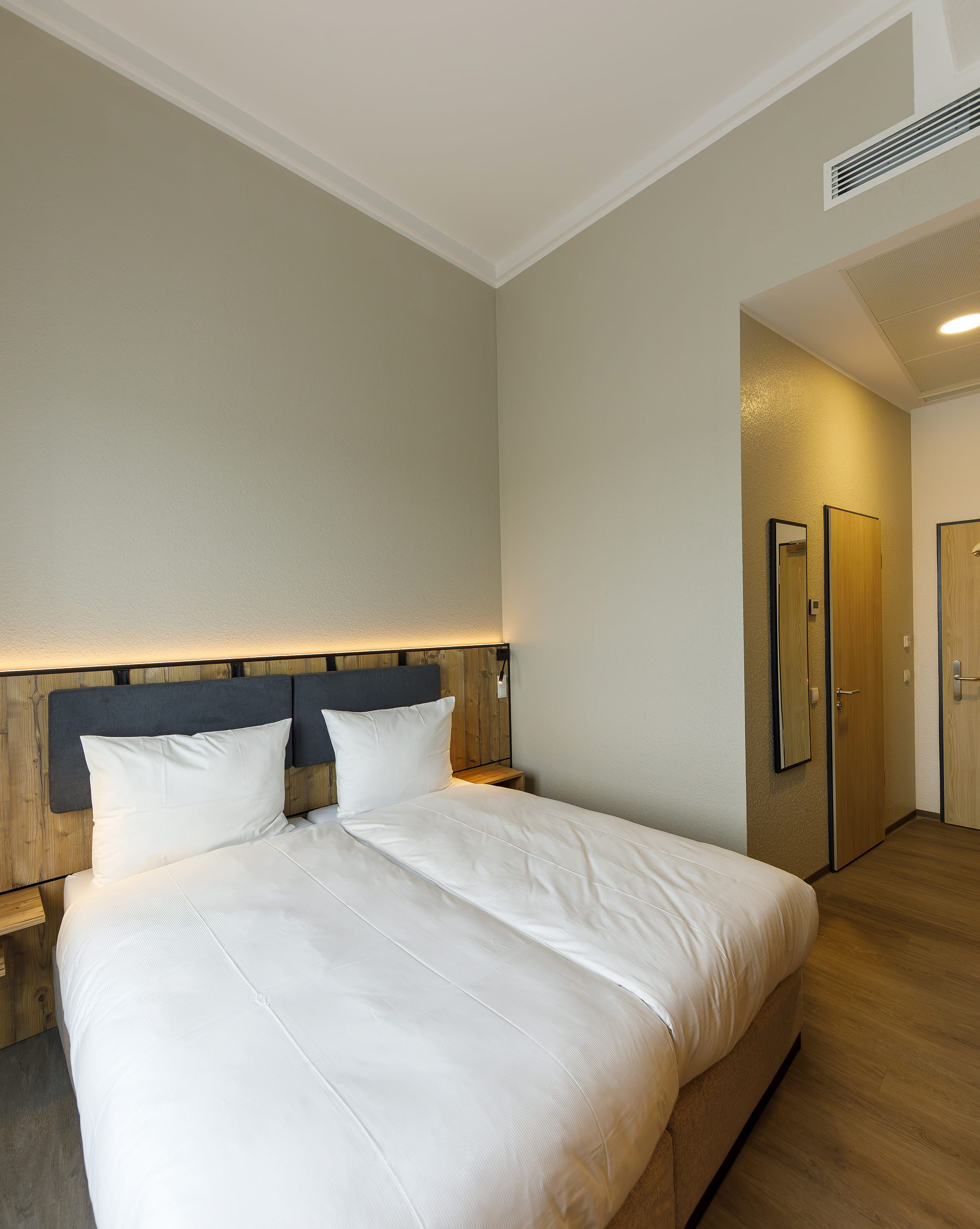 Quarto de hotel com cama grande, cabeceira de madeira e mesa de cabeceira.