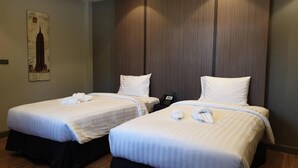 Quarto de hotel com duas camas, cada uma com roupa de cama e toalhas brancas, piso de madeira e telefone fixado na parede.