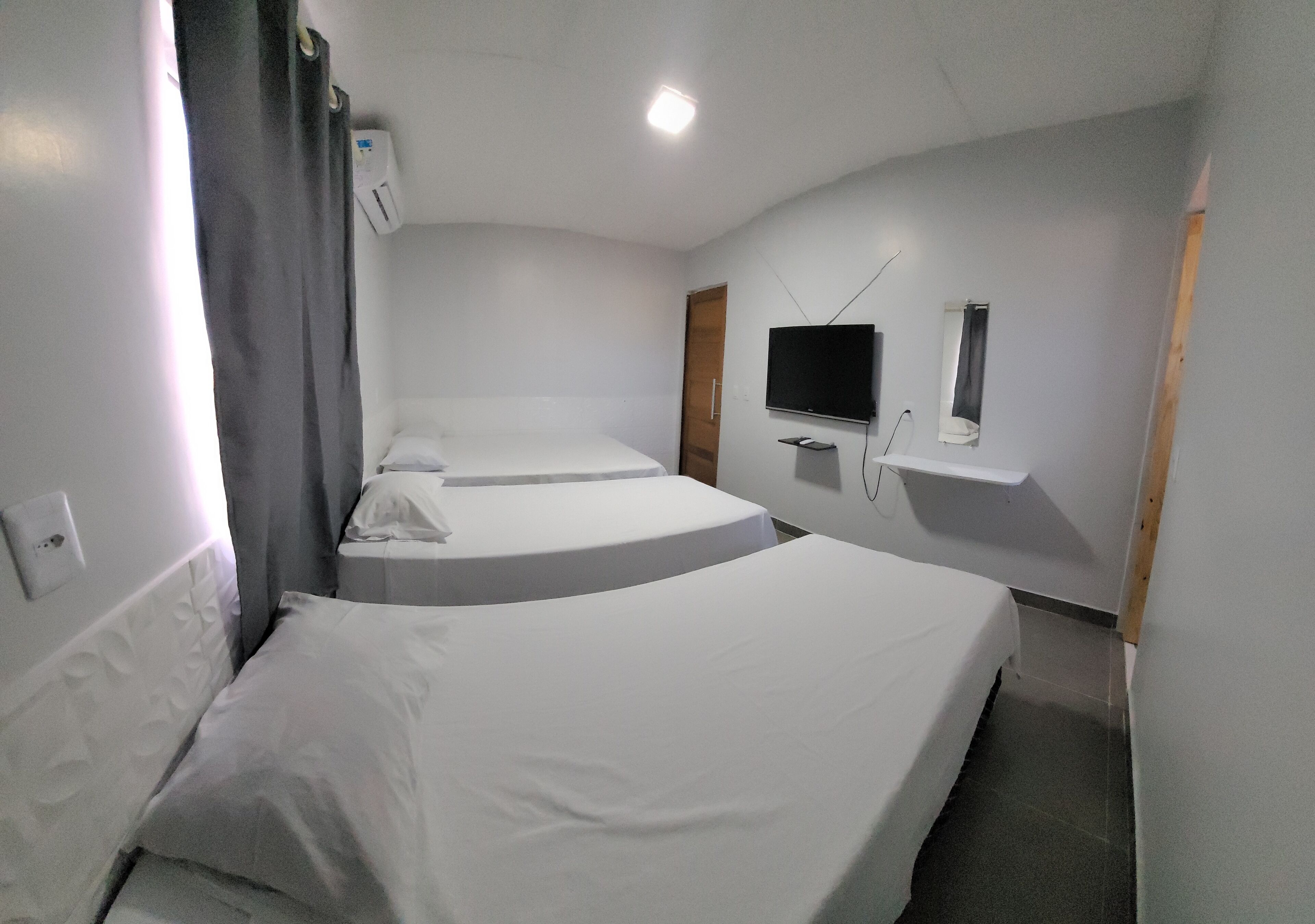 Quarto de hotel com duas camas, uma televisão de tela plana na parede e uma pequena janela com cortina.