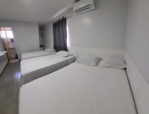 Quarto de hotel com três camas de solteiro, banheiro e janela com cortinas.