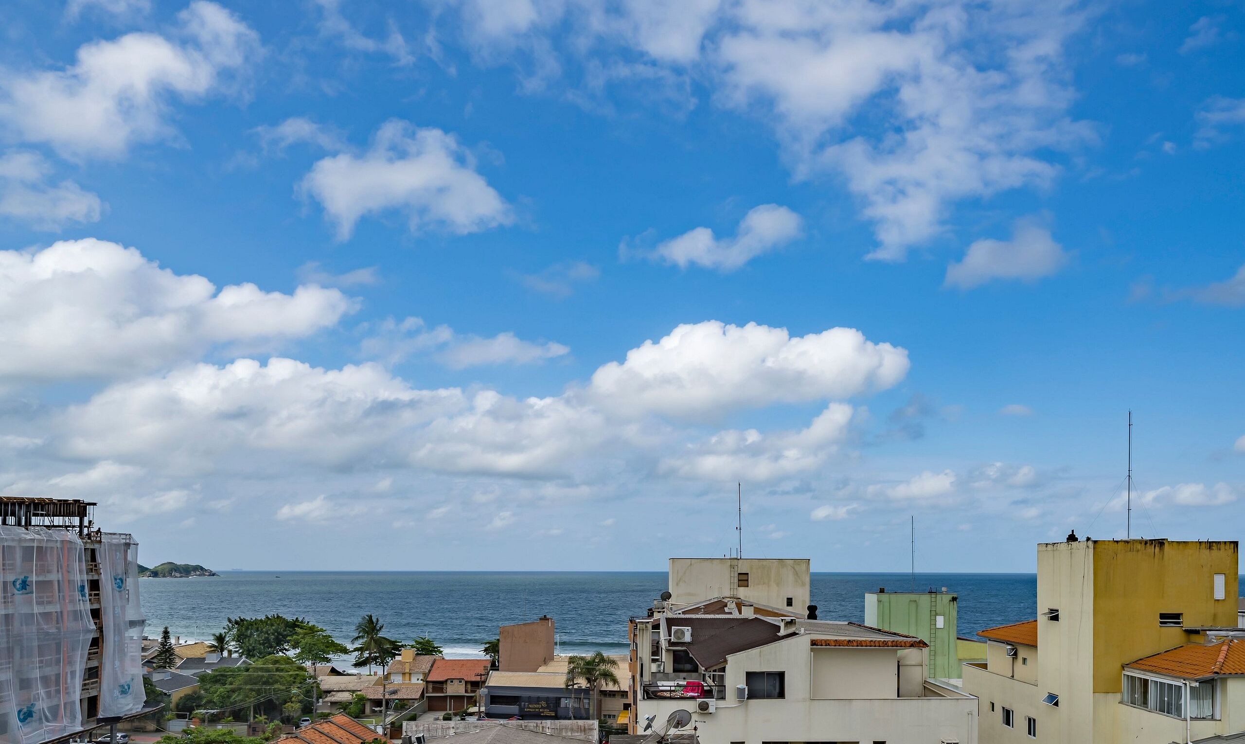 Uma área urbana costeira com edifícios, céu claro e o mar ao fundo.