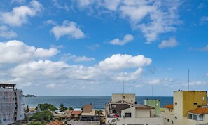 Uma área urbana costeira com edifícios, céu claro e o mar ao fundo.