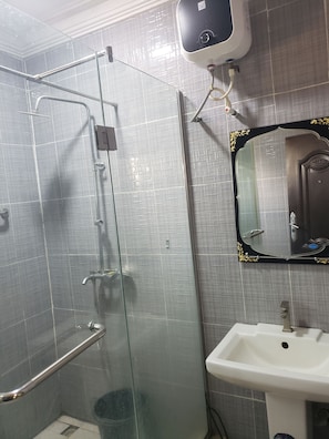 Casa de banho com cabine de duche em vidro, lavatório e espelho com moldura decorativa.
