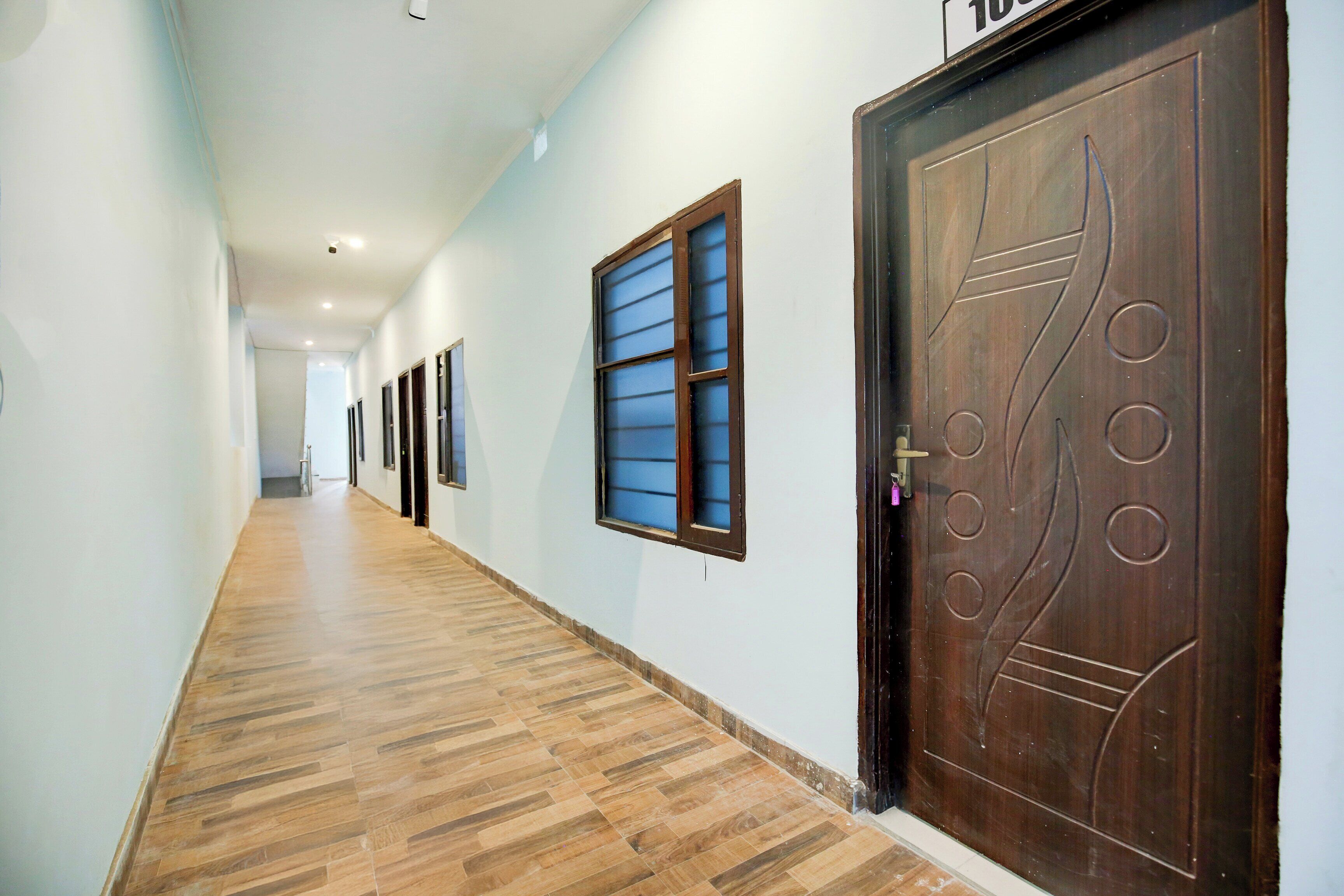 Um corredor com piso de madeira, uma grande porta de madeira com puxador circular e uma janela com persianas horizontais.