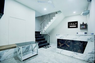 Um interior moderno com um balcão de recepção de mármore, uma vitrine de vidro e uma escadaria para um andar superior.